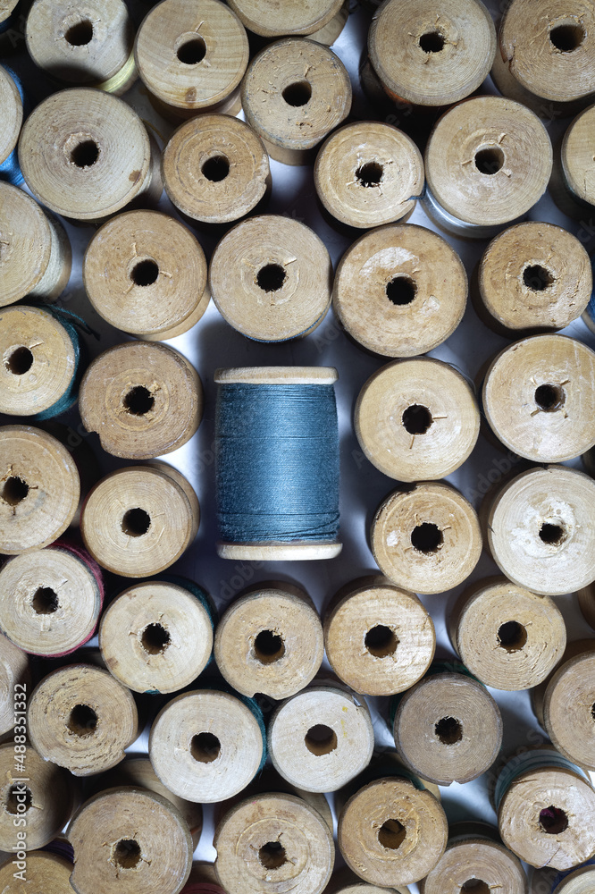 Wooden spools of thread are laid out around a blue bobbin of thread. A ...
