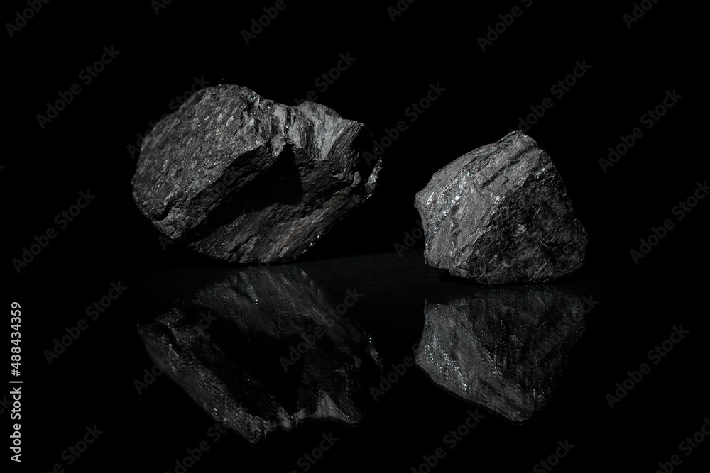 Black textured stones on a dark background lie on a glass surface and ...