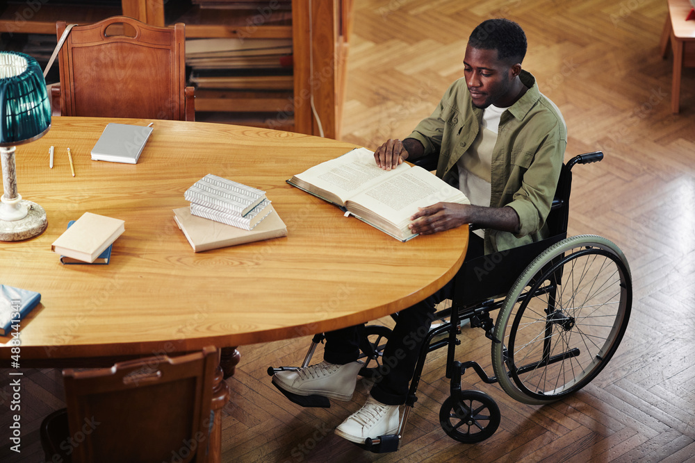 High angle portrait of young black student using wheelchair in library ...