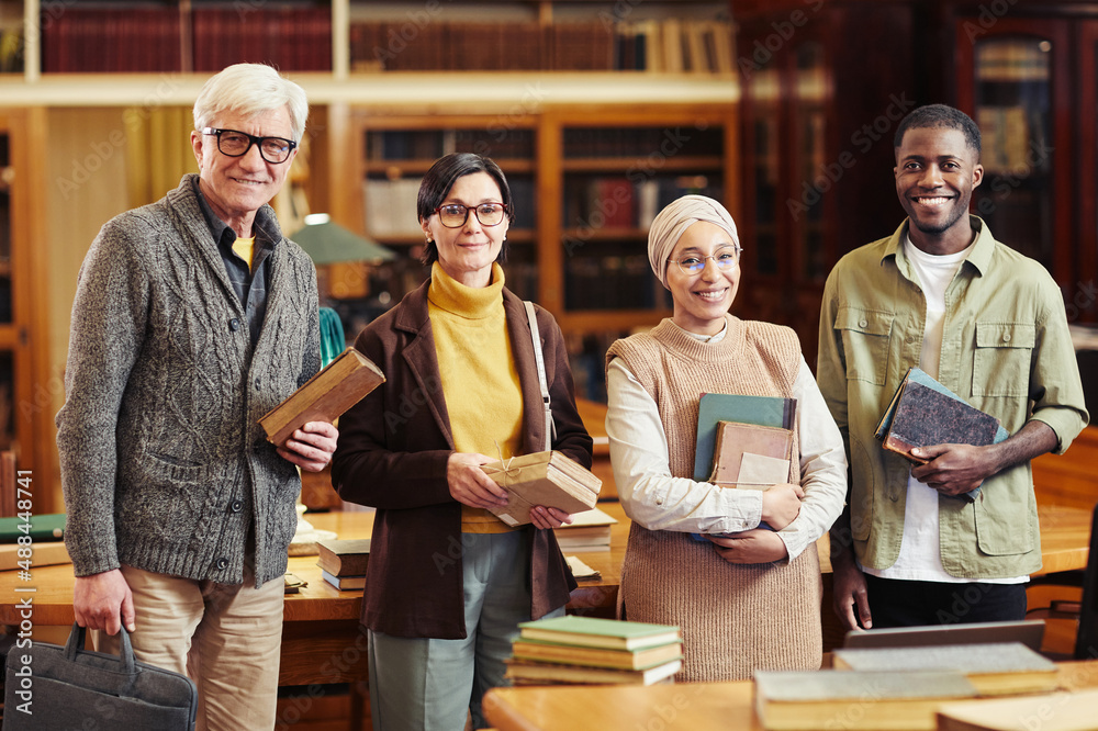 Diverse group of people holding books in classic library and looking at ...