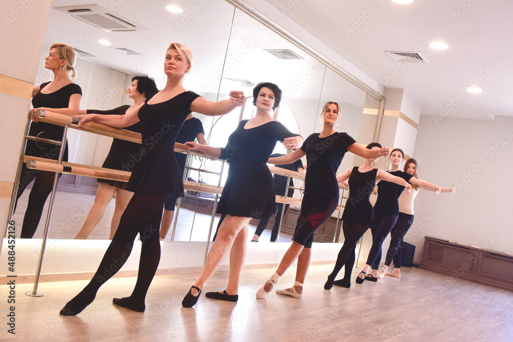 A group of women perform ballet exercises by raising their arms up ...