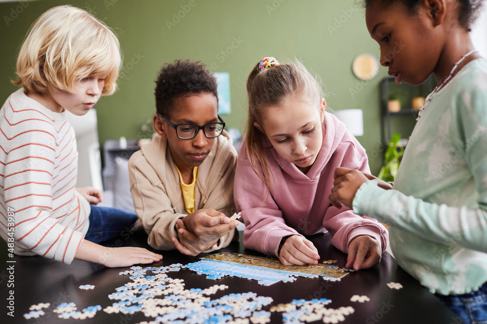 Portrait of diverse group of children playing with puzzle game indoors ...
