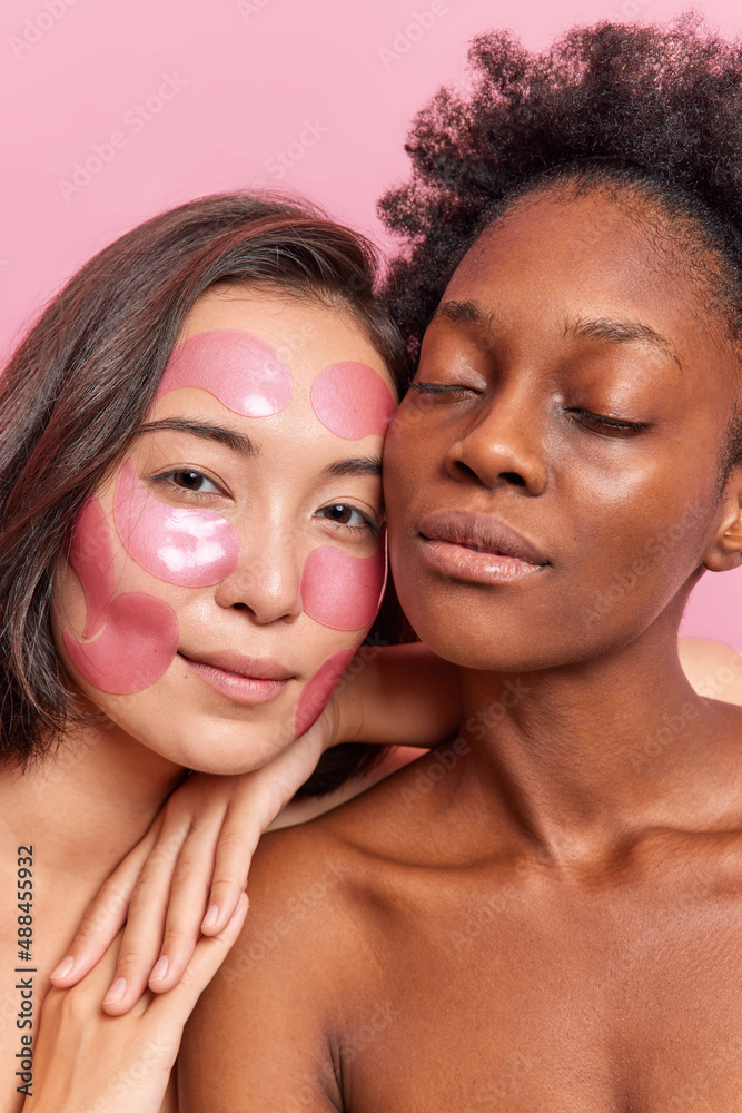 Vertical shot of two young women stand shirtless closely to each other ...