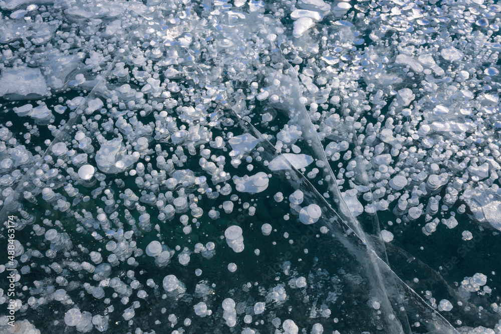 tiny frozen methane gas bubbles trapped under ice with fracture lines ...