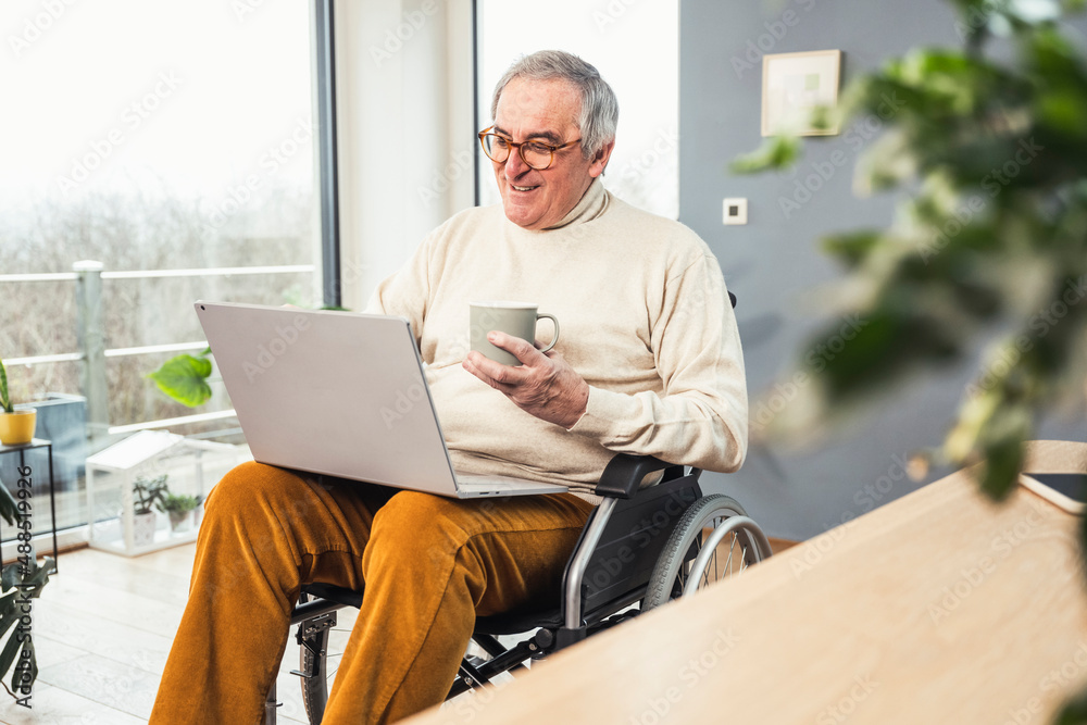 Smiling disabled senior man holding coffee cup using laptop sitting on ...