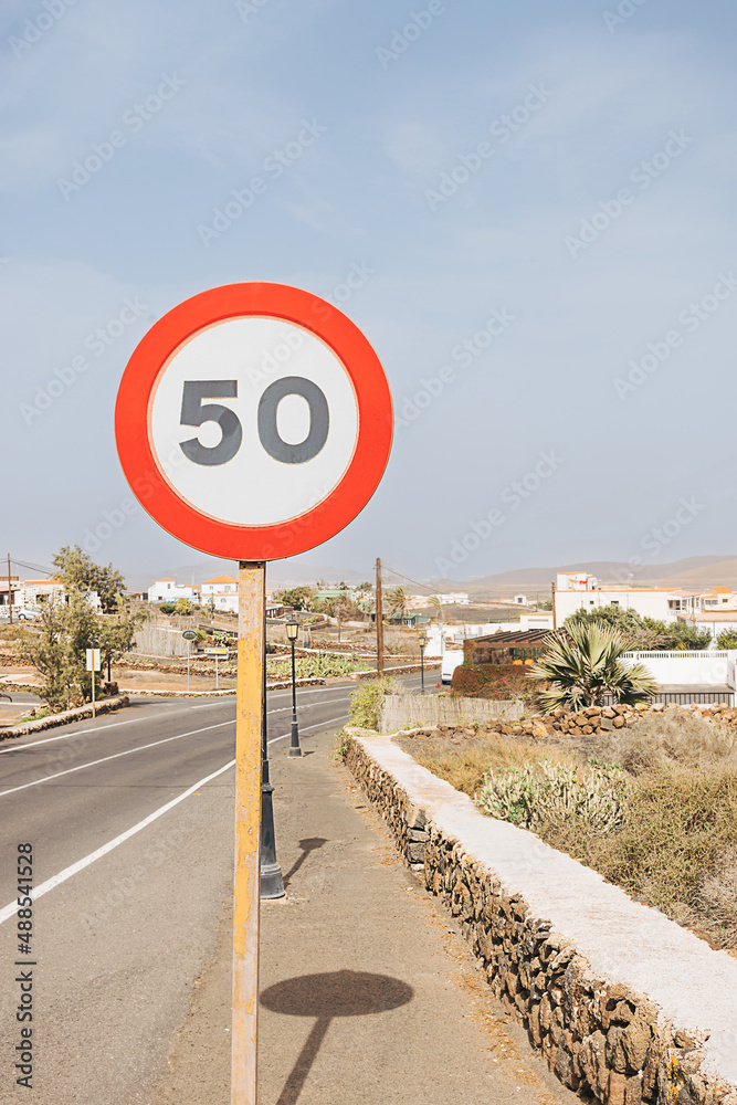 Round red speed limit road sign fifty on an empty tropical rural ...