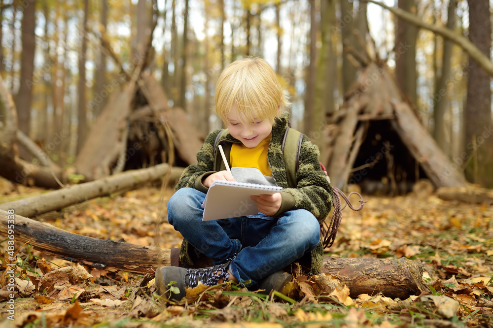 Little boy scout is orienteering in forest. Child is sitting on fallen ...