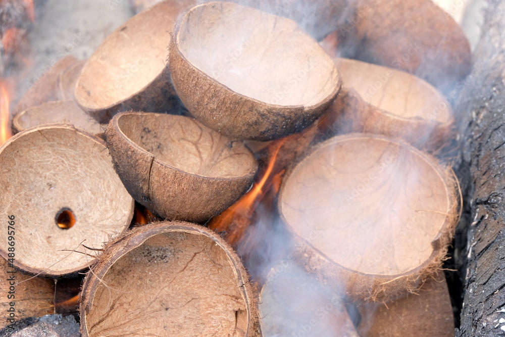 Pile of brown coconut shells on outdoor fire with flames and smoke ...