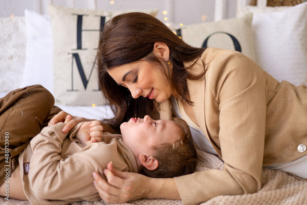 a mother with a small baby boy play, hug and kiss at home on a bed in ...