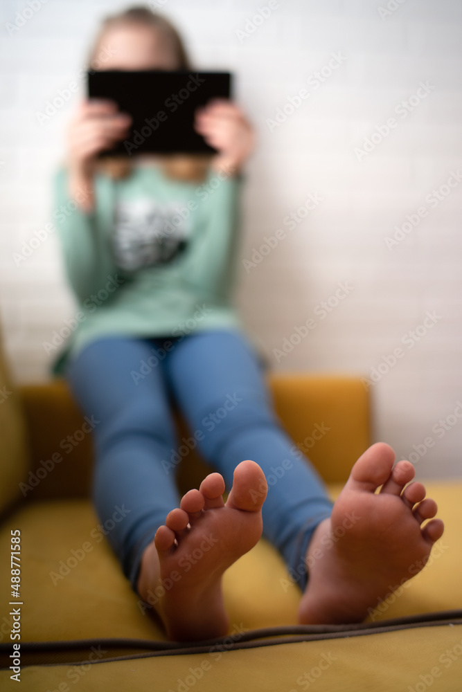 Foto Stock girl sits on a yellow sofa and uses a gadget tablet, close ...