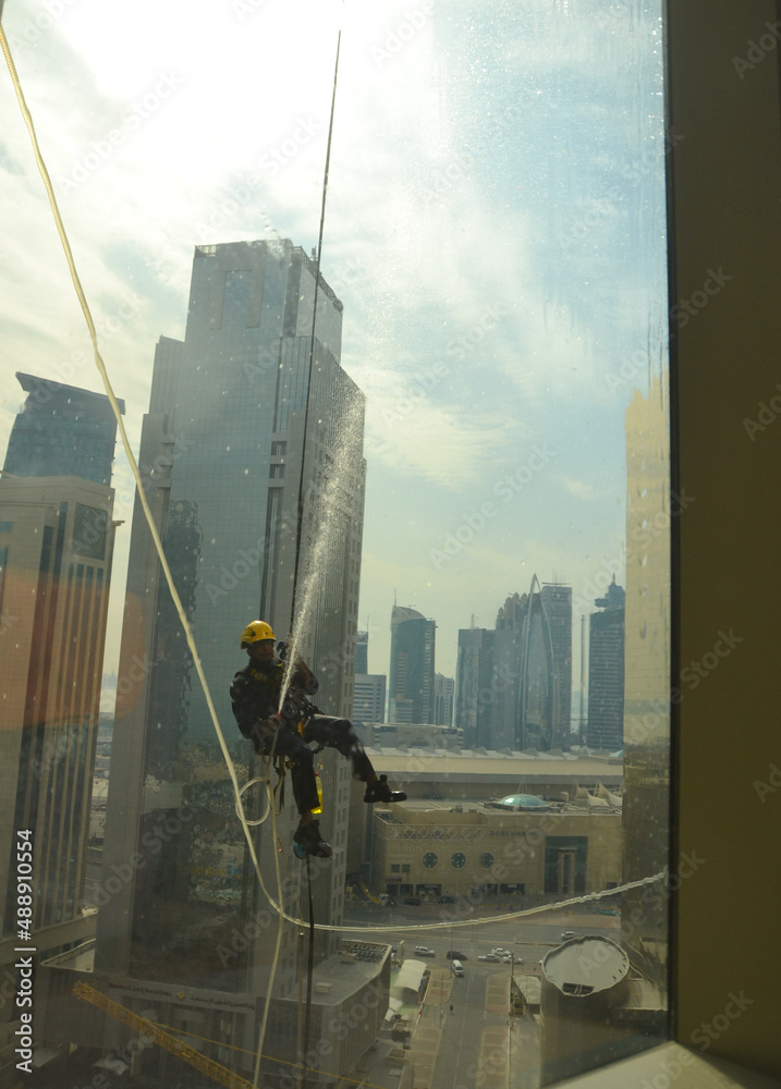 Skyscraper window cleaner hanging from a harness in Doha, Qatar. View ...