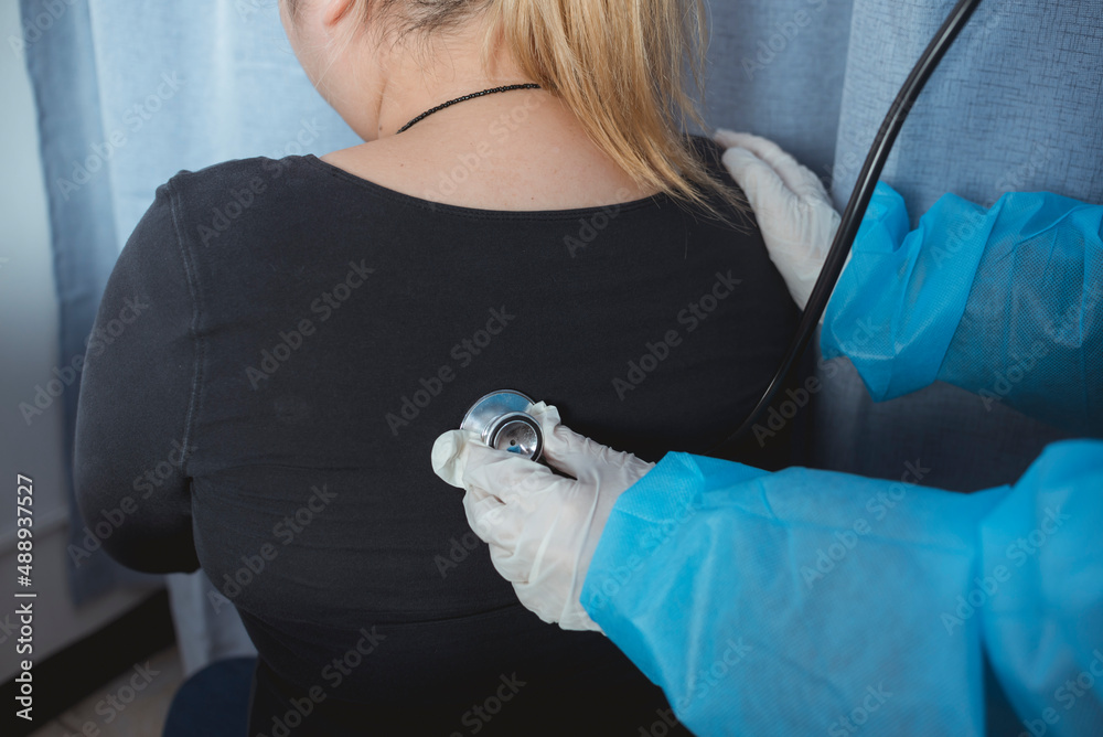 An anonymous doctor checks a patient's breathing with a stethoscope on ...