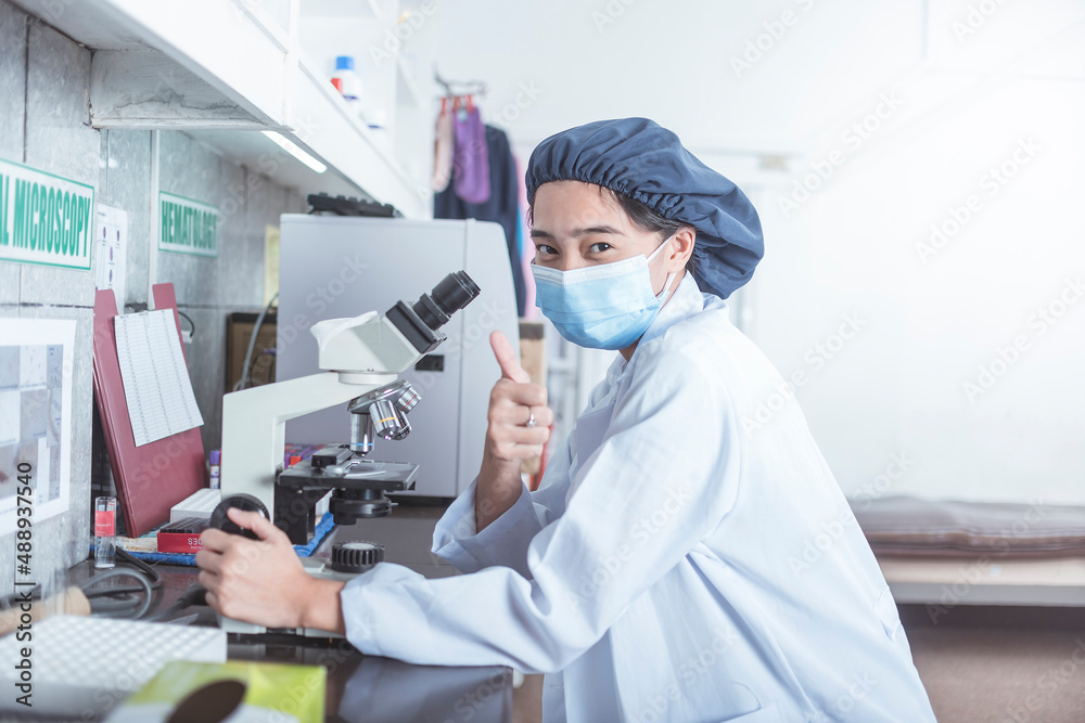 A cheerful asian laboratory technician making a thumbs up while ...