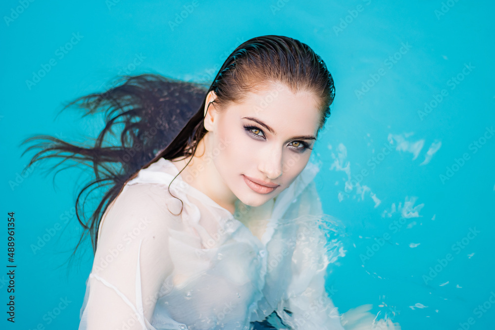 Top view, portrait of a young, beautiful woman floating in the pool, wearing a white shirt. Rest ...