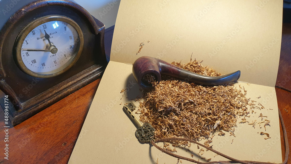 wooden smoking pipe on top of an old book and a table clock among loose ...