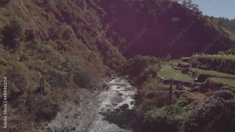 two people hiking trekking across metal wire suspension bridge spanning ...