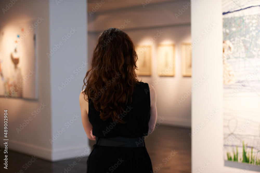 Taking in a century of art. Shot of a young woman looking at paintings ...