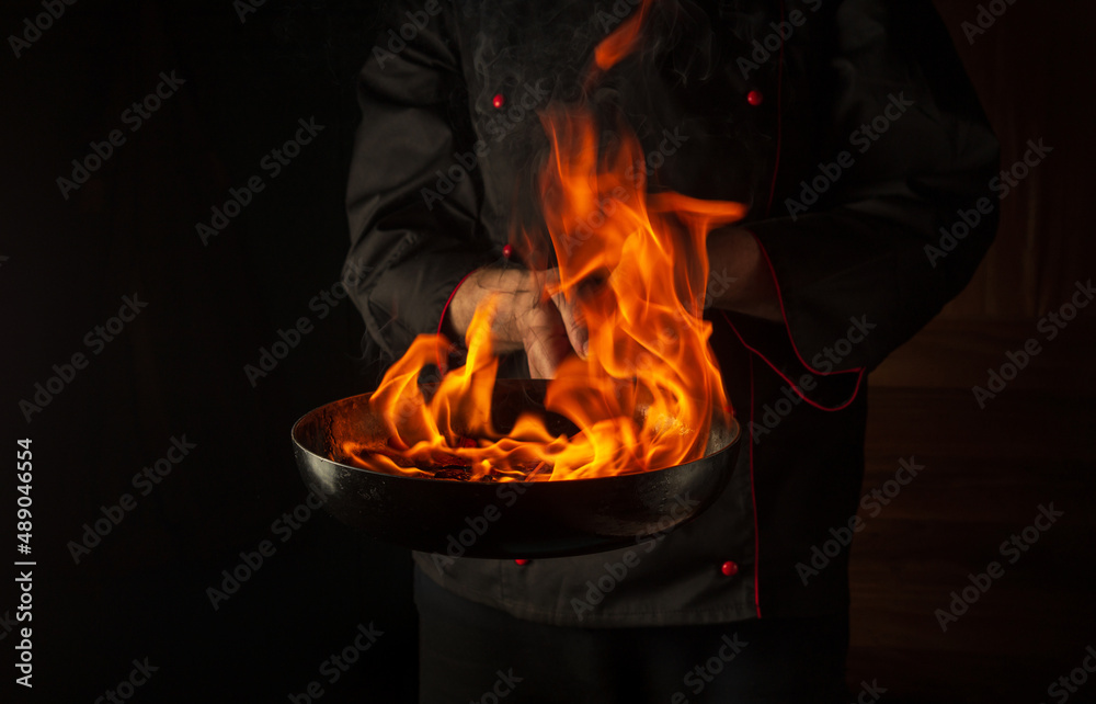 Professional chef cooking food in pan with fire flame on black ...