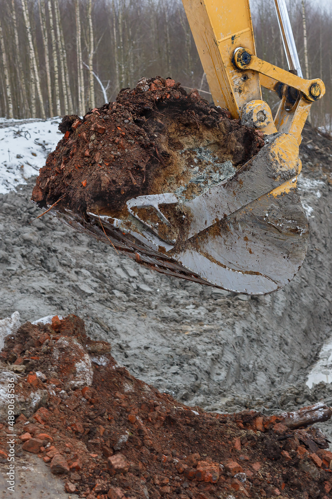 the process of loosening frozen winter soil with an excavator bucket ...