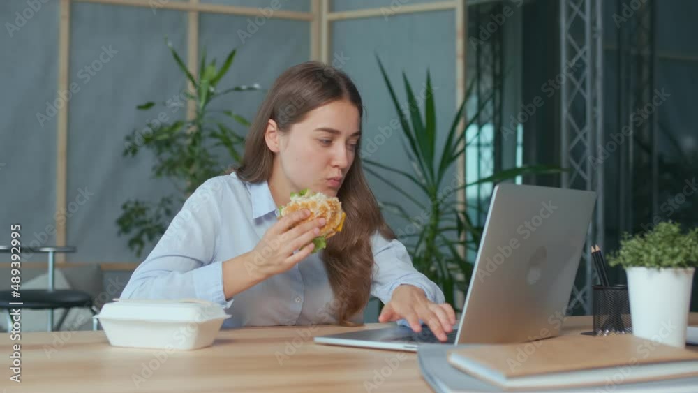 Young Businesswoman Eating Hamburger while Working on Laptop at the ...