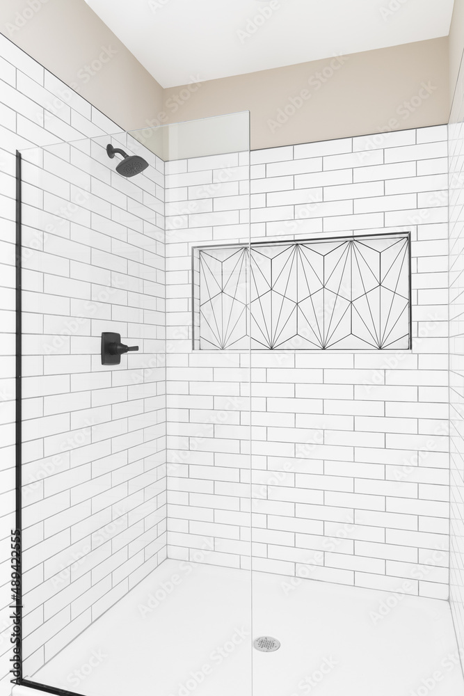 A renovated shower with white subway tiles, glass wall, black faucet ...