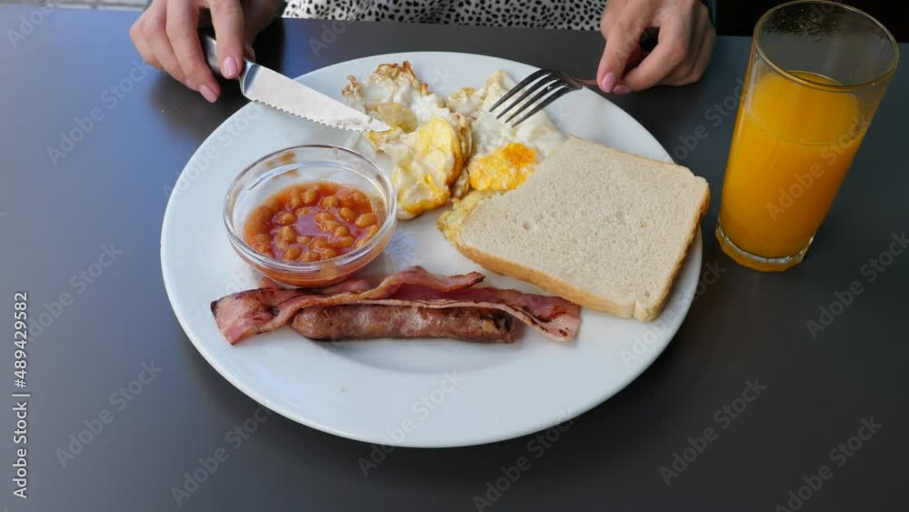 Woman sit still with fork and knife in hands over plate with breakfast ...