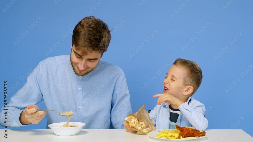 A man and a boy are sitting at the table, the man is eating porridge ...