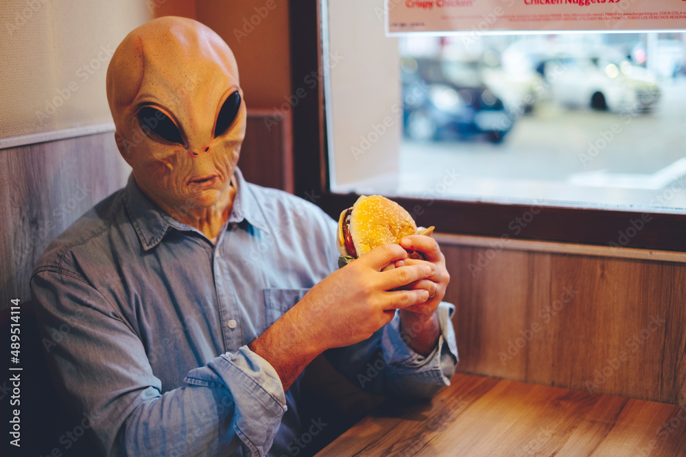 Alien with human clothes eating hamburger sandwich inside a fast food ...