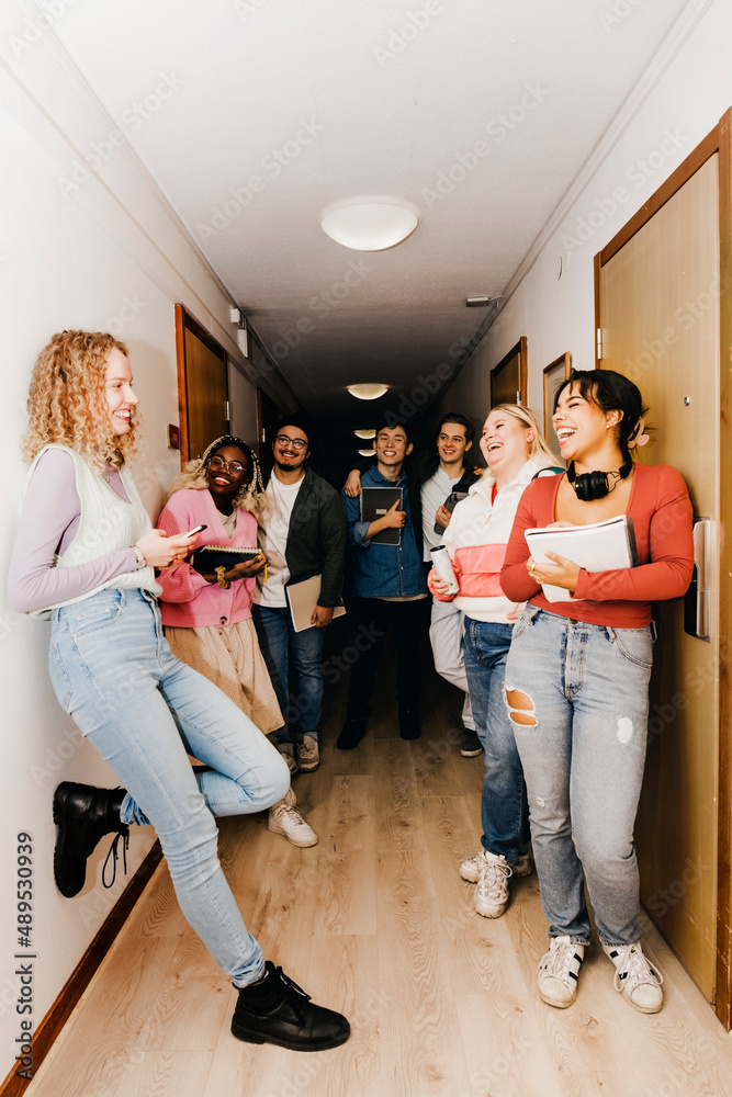 Multiracial students looking at female friend and laughing at corridor ...