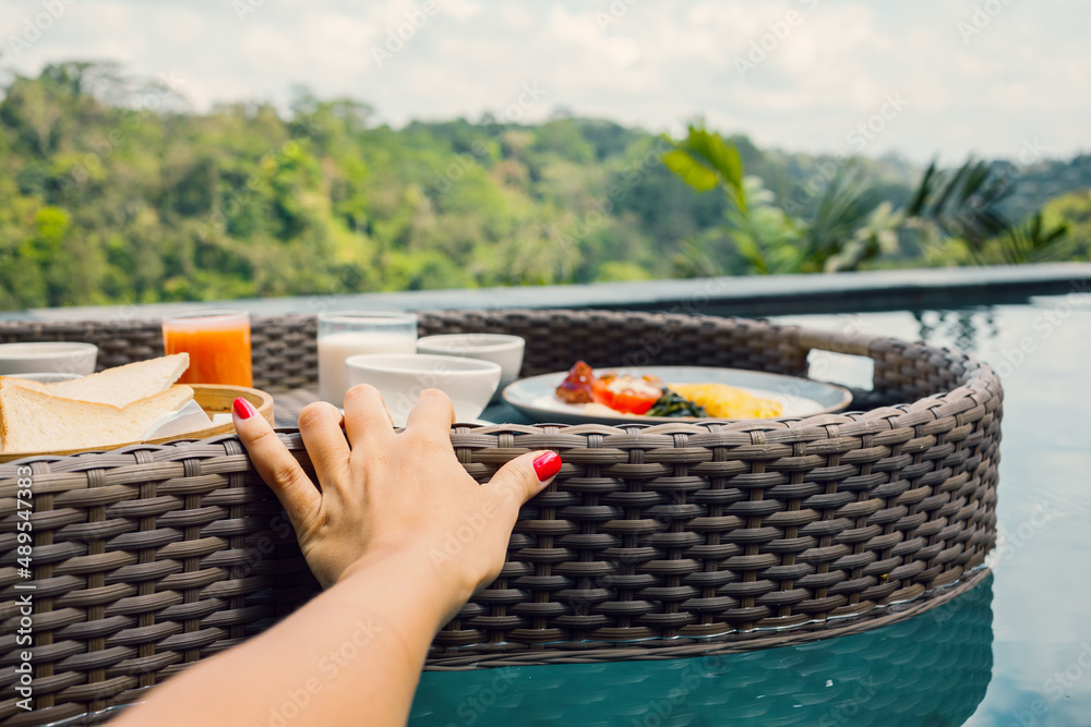 Girl dragging floating tray with food in swimming pool overlooking the ...