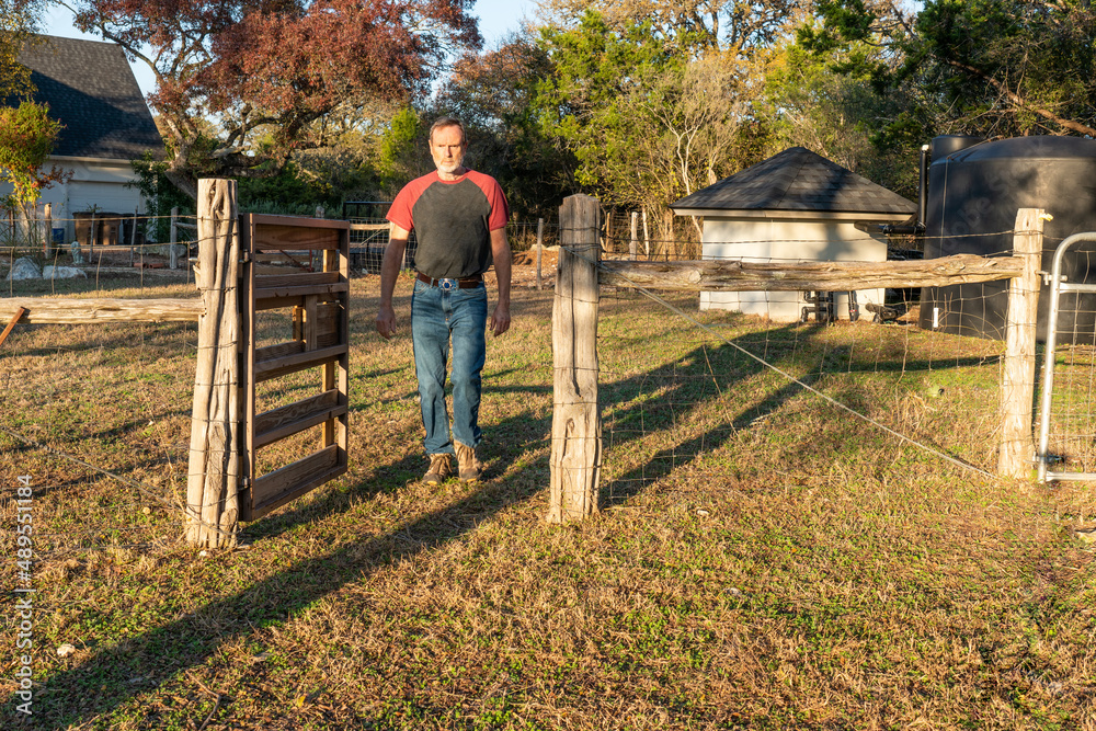 Caucasian man person walking through an open gate in a Texas field wire ...