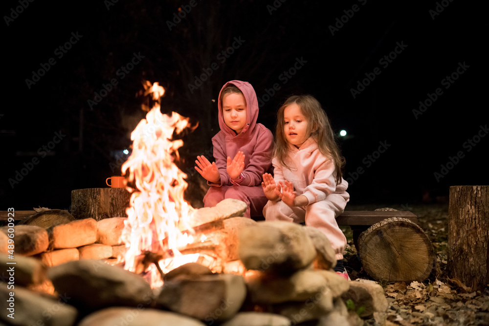 Children learning the basics of building campfire. Girls warming their ...