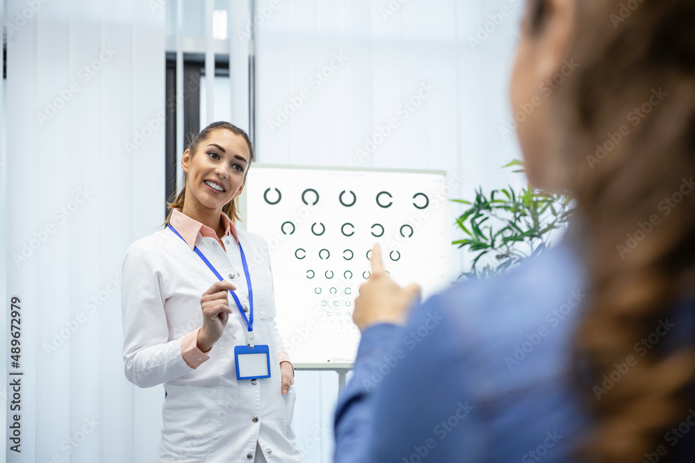 Professional female optician pointing at eye chart, timely diagnosis of ...