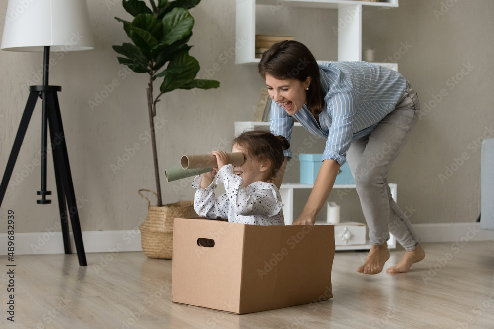 Joyful laughing young mother pushing cardboard box with seated little ...