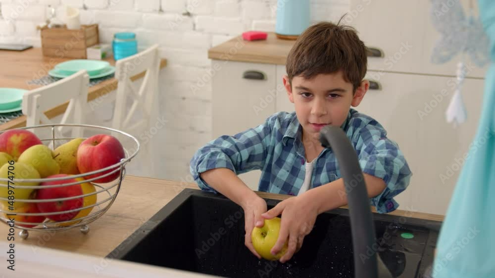 7-8 years old caucasian boy washes an apple in the sink of a modern ...