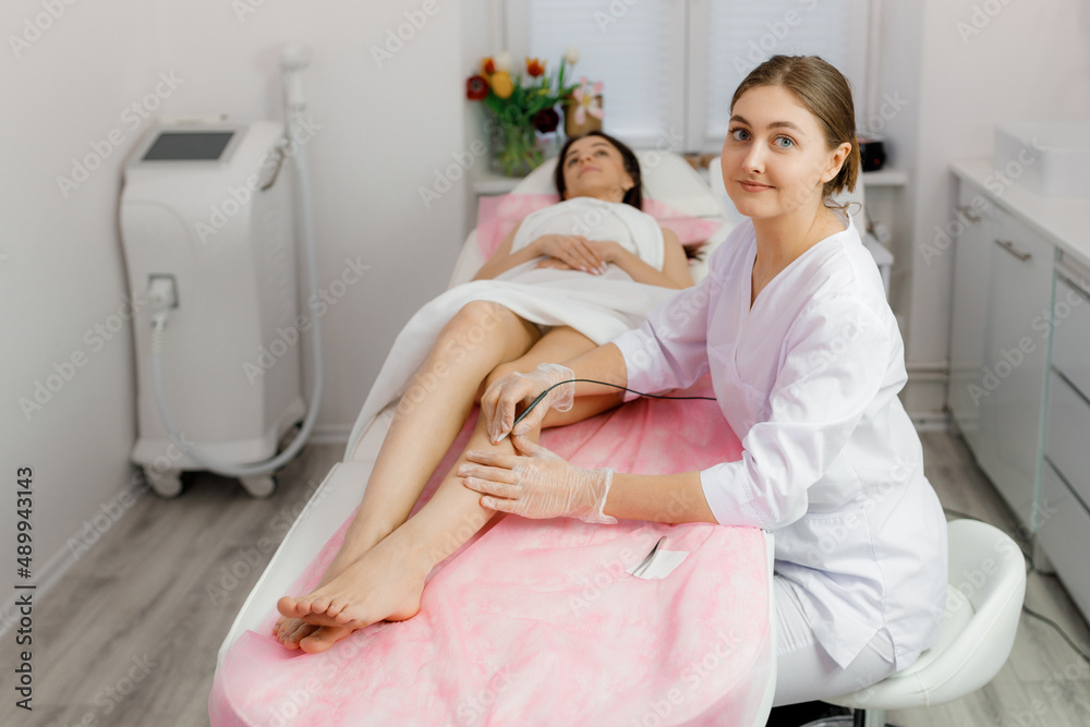 Dermatologist doing hair removal treatment on patient's leg with ...