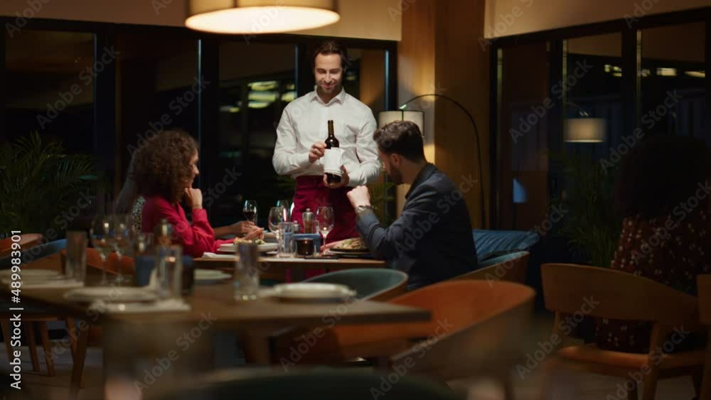 Waiter pouring wine bottle to fancy couple table at night restaurant ...