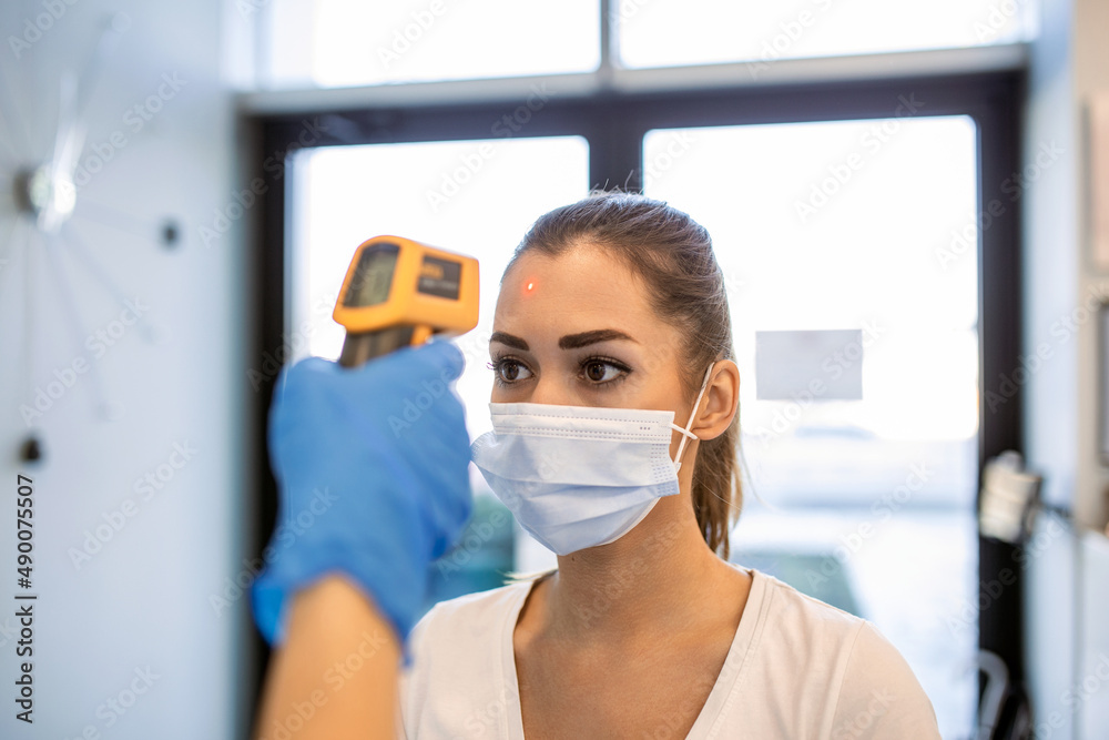 Nurse checking woman's temperature with infrared thermometer at counter ...