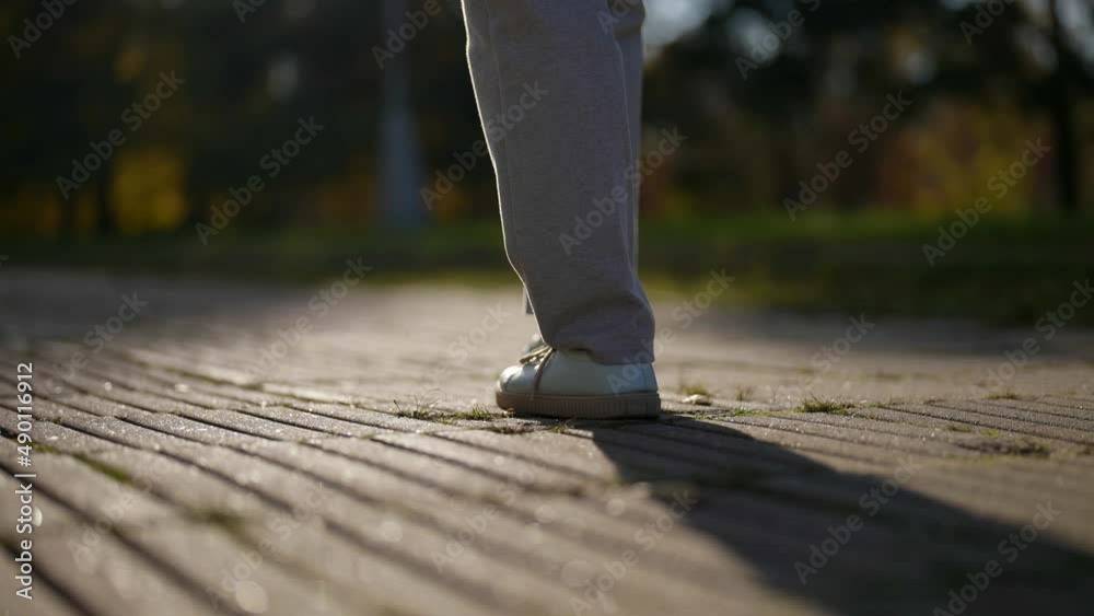 Close-up of a woman feet walking on the sidewalk in a city park. An ...