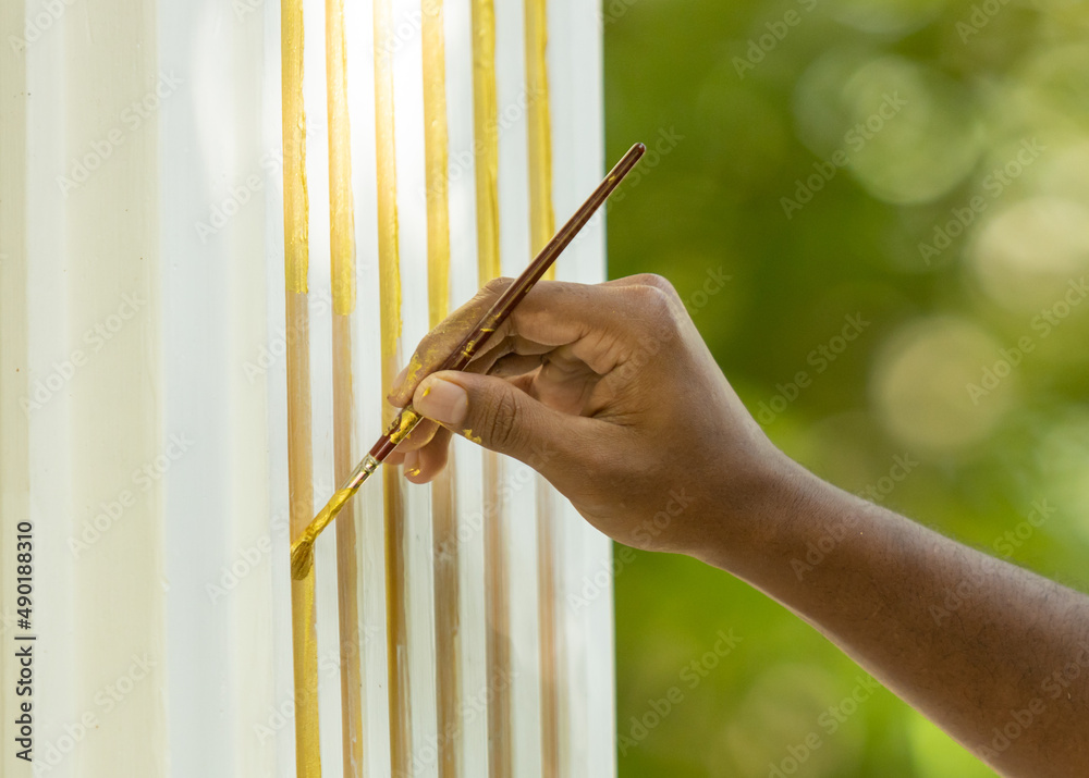 Male hand painting the vertical lines on the wall with a golden paint ...