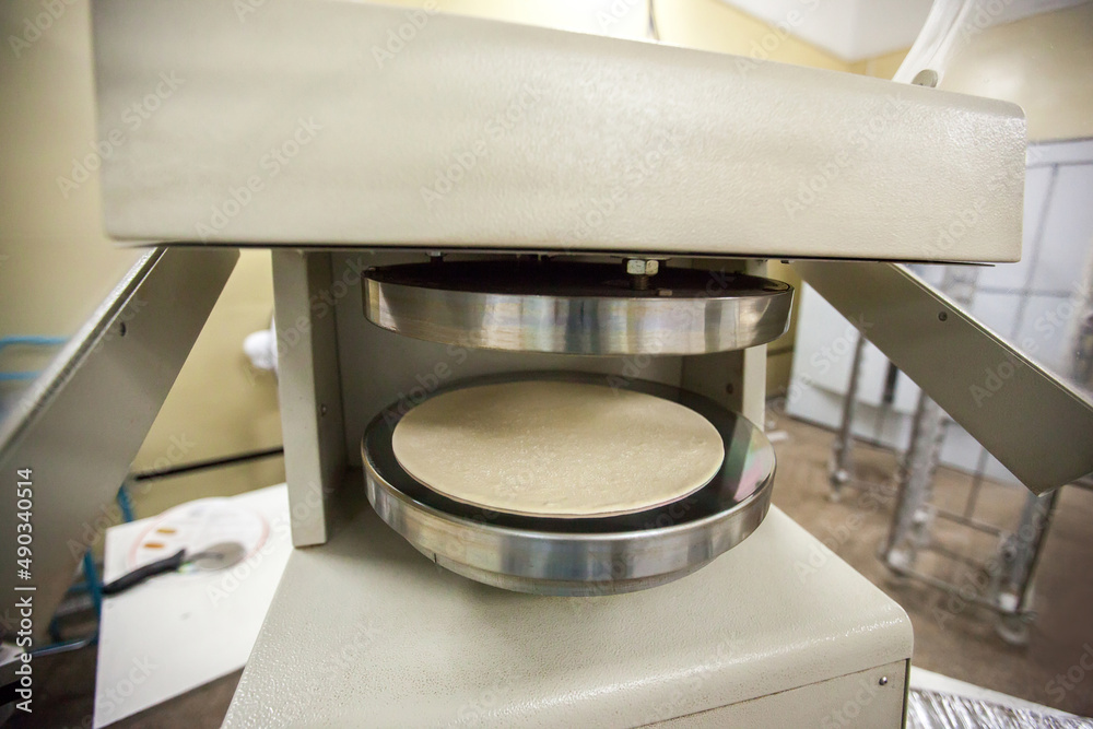 Cooking the pizza base at the factory. Automated dough rolling. Stock ...
