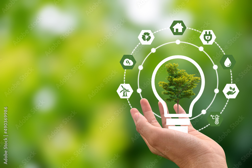 Hand holding light bulb icon and saving energy icon on green background ...