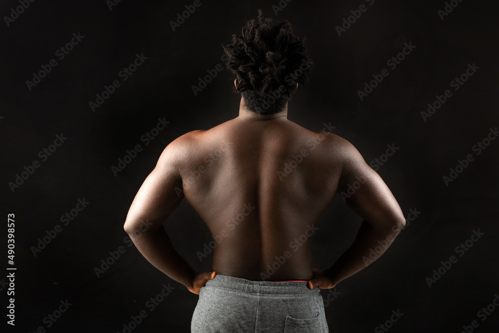 athletic figure of an African man standing with his back on a black ...
