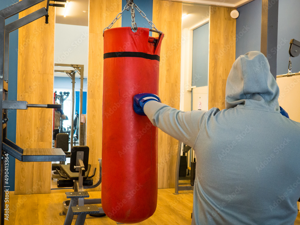 Boxing training - a hand and a red punching bag.a guy in a hood hits a ...