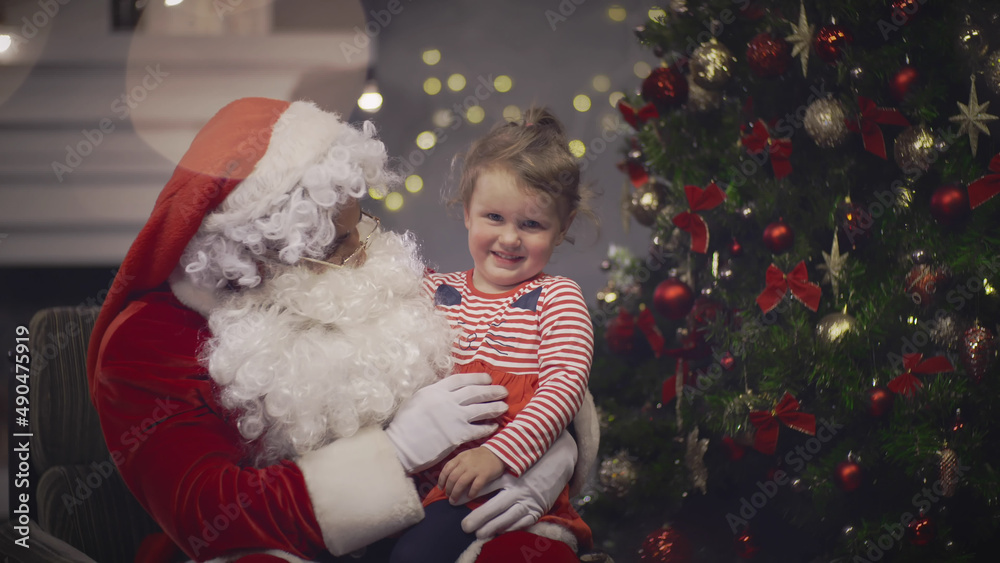 Kind Santa Claus playing with little girl sitting on his lap near ...