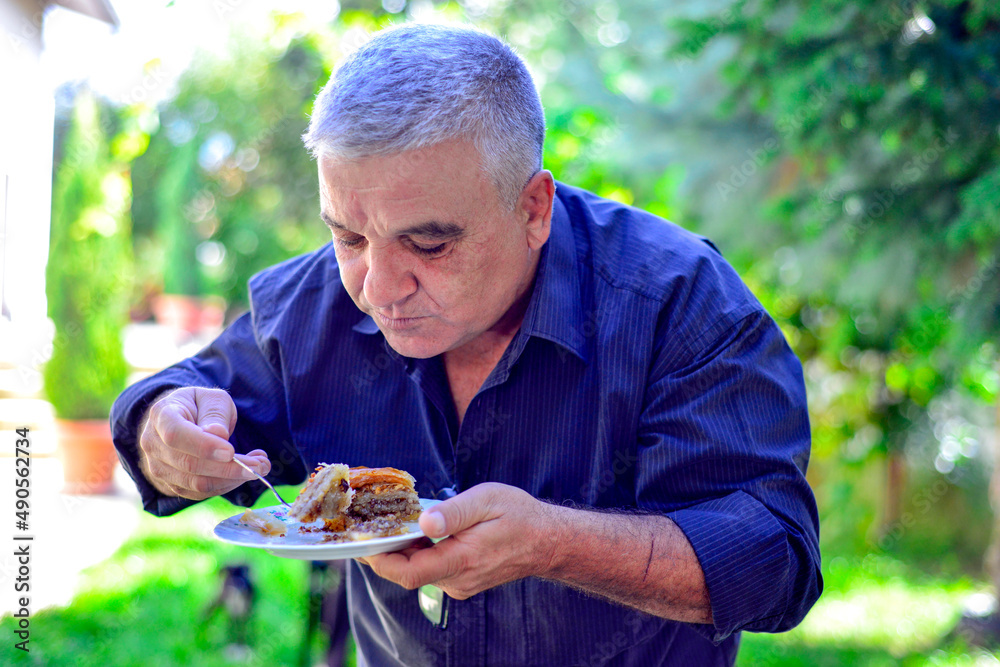 Man eating turkish baklava on a plate on sunny summer day in a backyard ...
