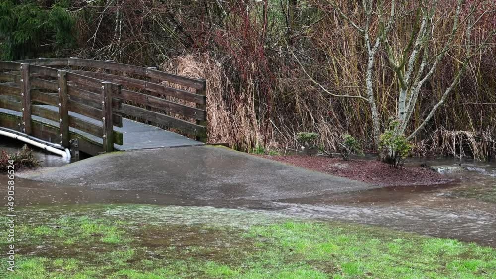 Pedestrian bridge and path with excess rainwater overflowing the stream ...