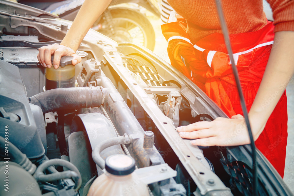 Professional Asian female mechanic in a red uniform checks the oil level of the diesel pickup ...