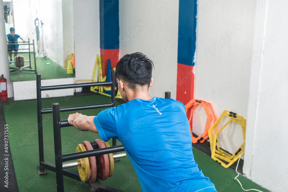 A young man uses a sled push at the gym. A prowler sled with weights ...