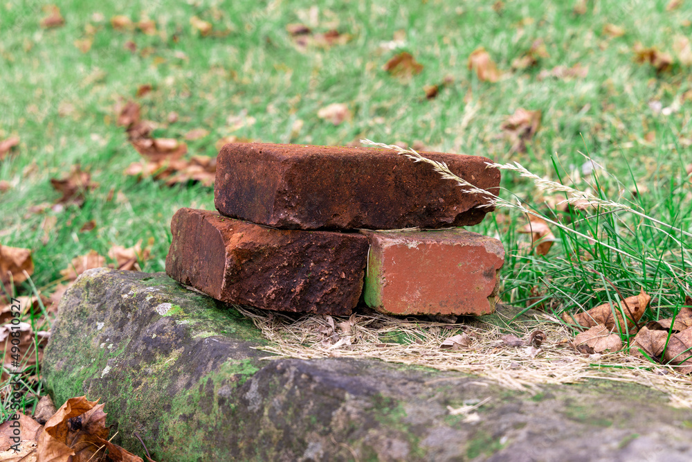 Red bricks placed on an old stone covered with moss with green grass on ...